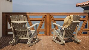 Duas cadeiras de balanço em um deck de madeira, com vista para o mar.