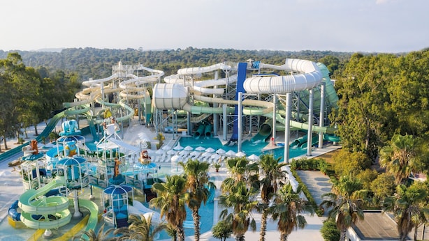 Um parque aquático com várias piscinas e toboáguas, cercado por palmeiras e vegetação.