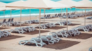Uma praia com fileiras de espreguiçadeiras e guarda-sóis.