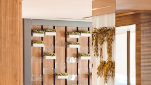 Um interior moderno com área de estar, com duas cadeiras brancas e uma mesa, divisória de madeira com ripas verticais e uma planta pendente.