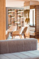 Um interior moderno com área de estar, com duas cadeiras brancas e uma mesa, divisória de madeira com ripas verticais e uma planta pendente.
