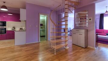 Um interior moderno com escada em espiral, piso de madeira, cozinha com armários roxos e um sofá rosa.