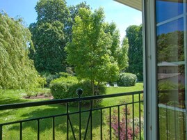 Um jardim com diversas árvores e arbustos, gramado e grade de metal.