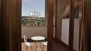 Uma varanda com mesa e cadeiras, vista para uma colina com um símbolo de coroa, e vigas de madeira.