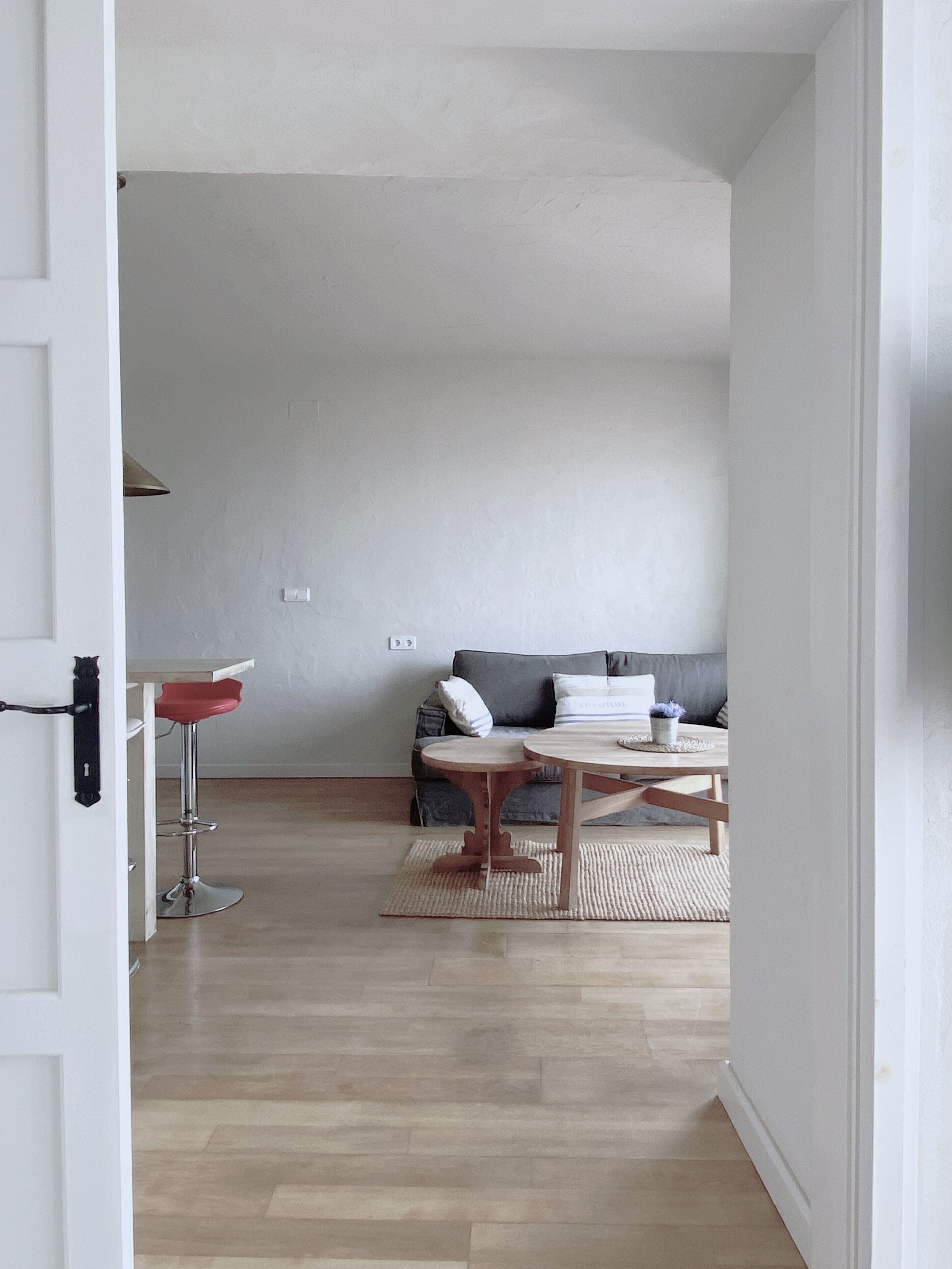 Uma sala moderna com piso de madeira, uma mesa de jantar com cadeiras, um sofá e uma pequena área de cozinha com um banquinho.