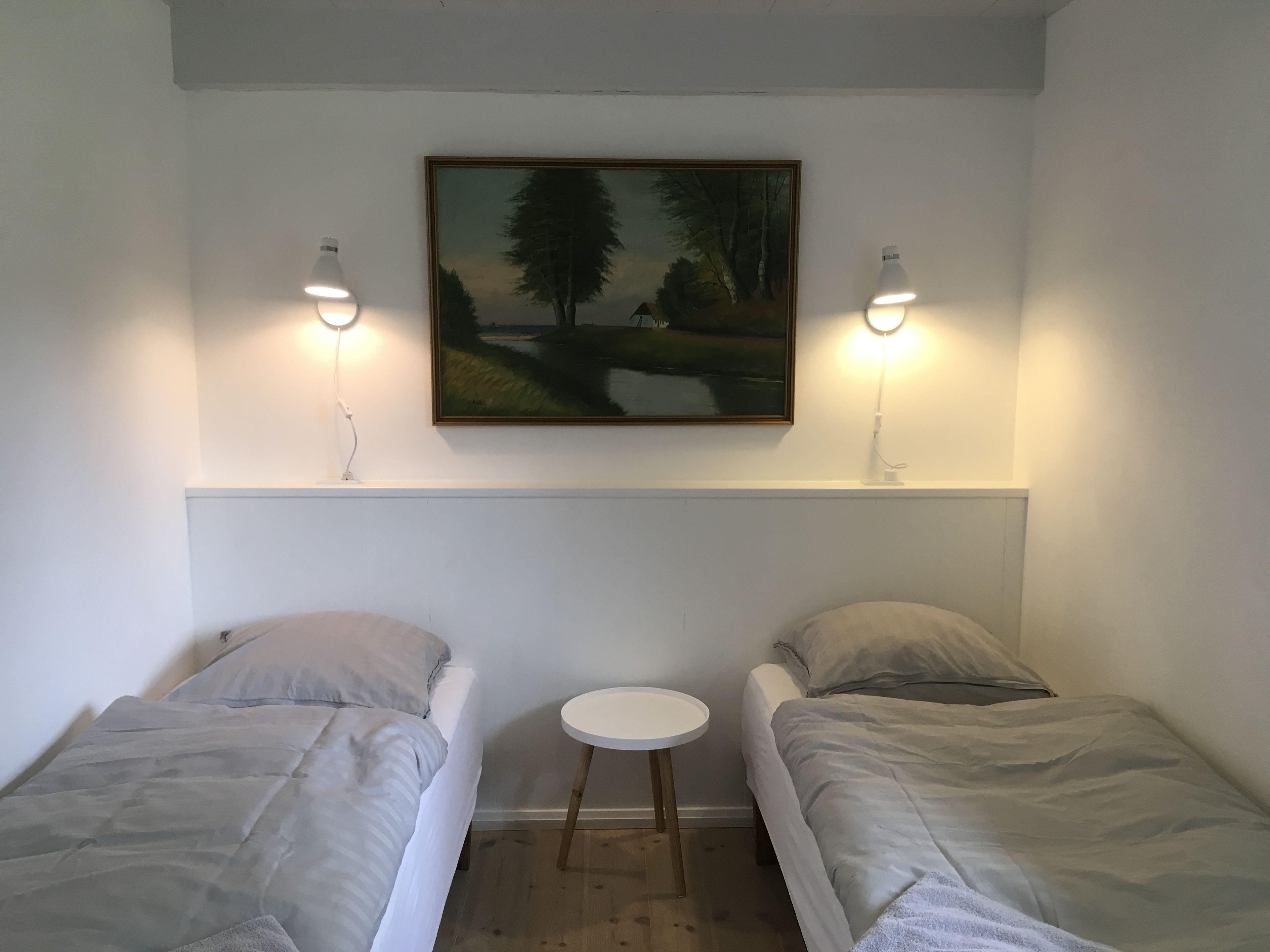 Quarto com duas camas de solteiro, uma mesa redonda pequena e um quadro na parede.