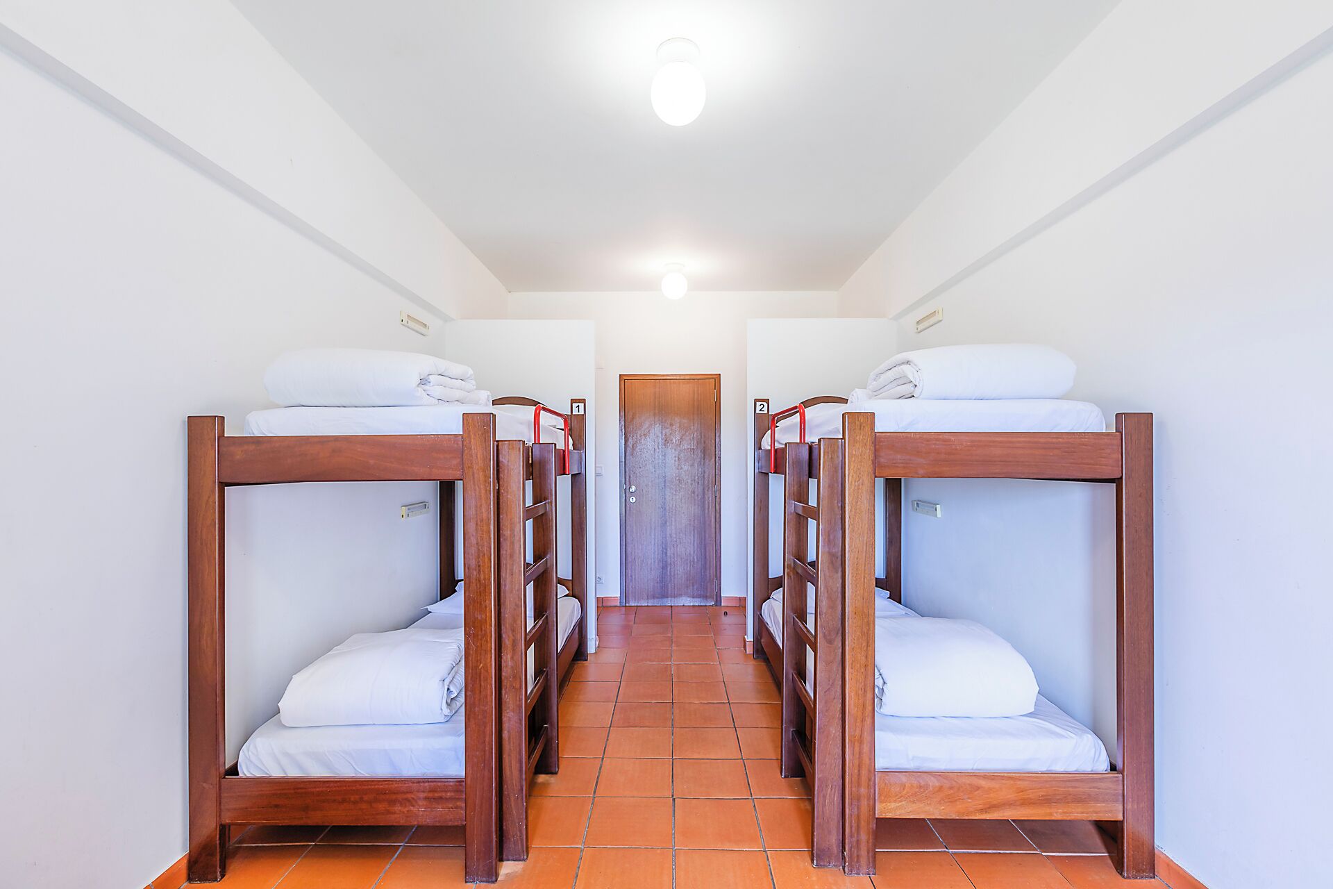 Corredor com beliches, uma porta e luminária.