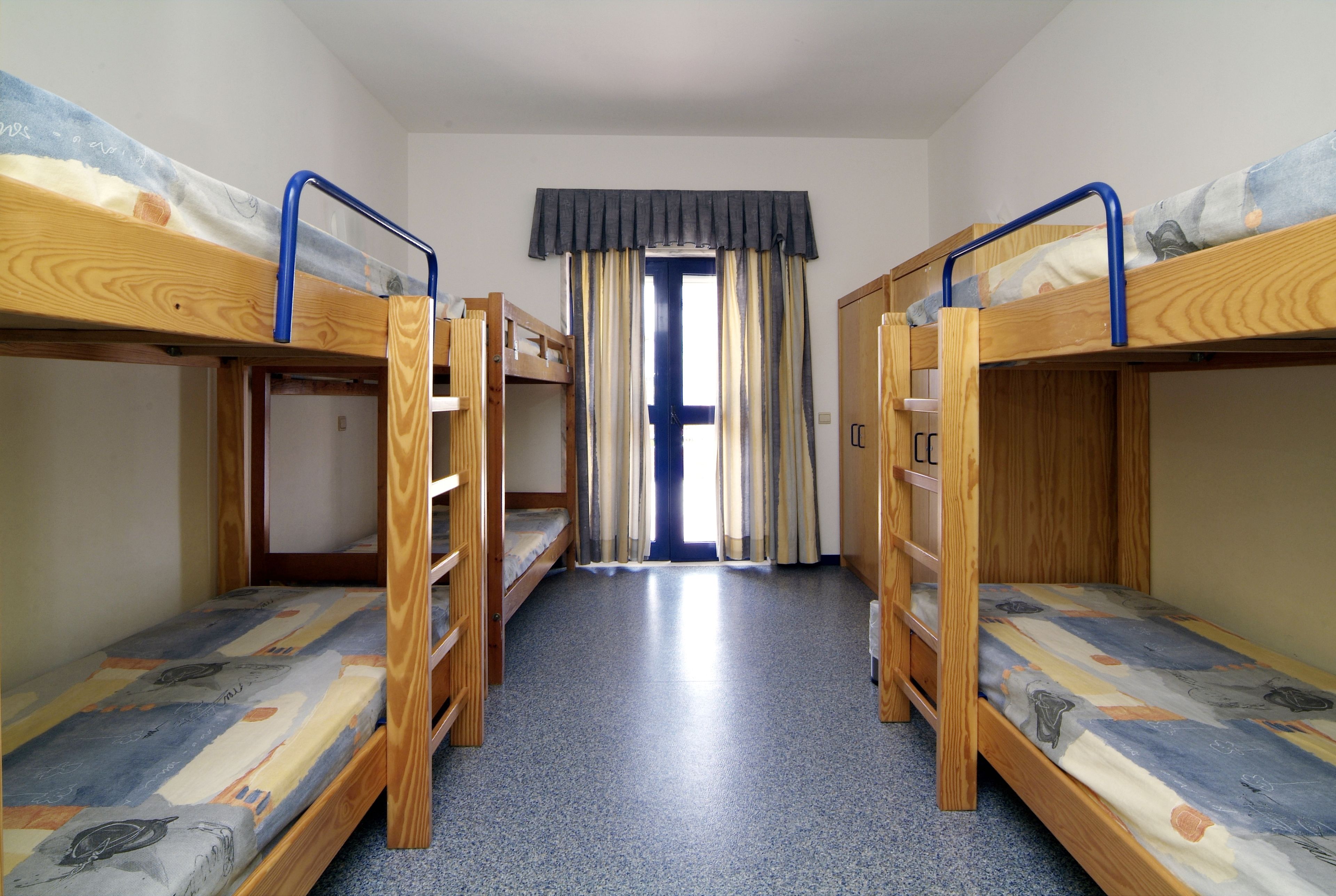 Quarto com beliches, janela com cortinas e uma porta.