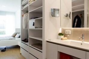 Quarto moderno com cama, armário embutido e banheiro com pia e espelho.