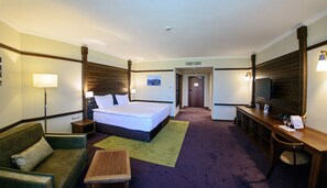 Quarto de hotel com cama, escrivaninha, televisão, sofá e uma mesinha.