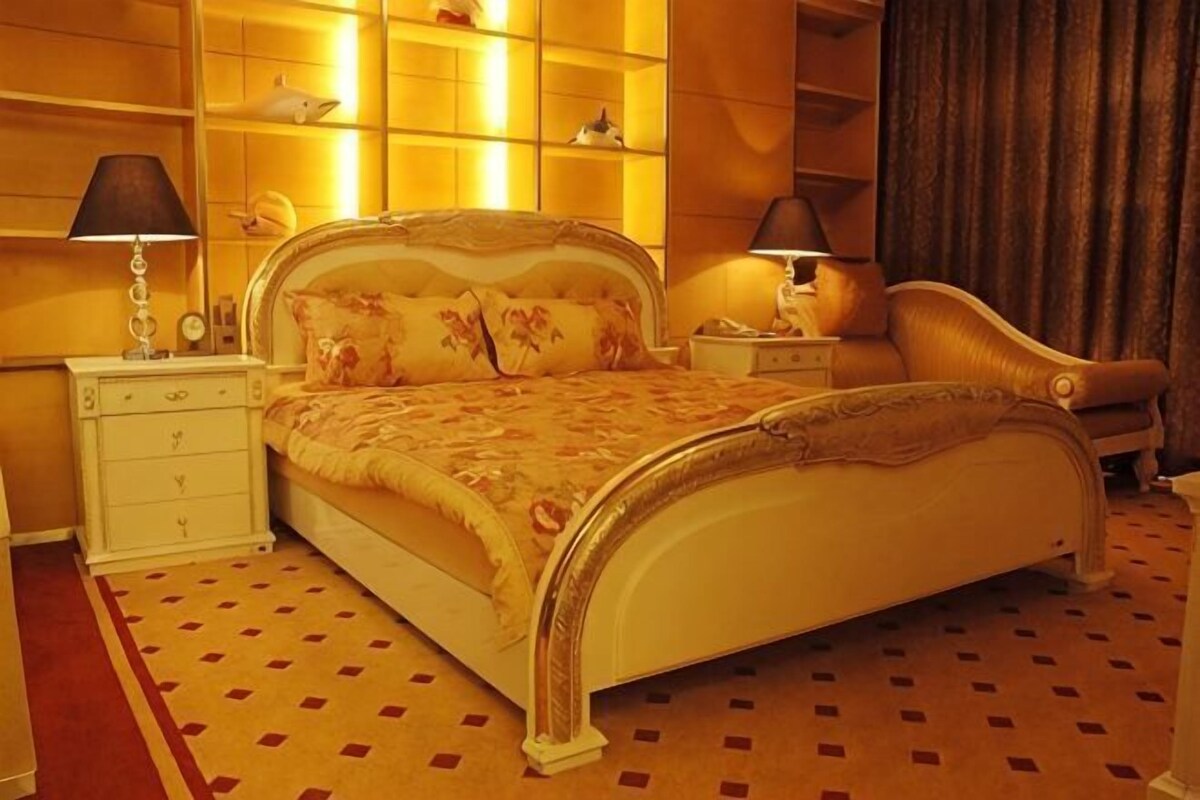 Quarto com cama, mesas de cabeceira, uma cadeira e uma estante com objetos decorativos.