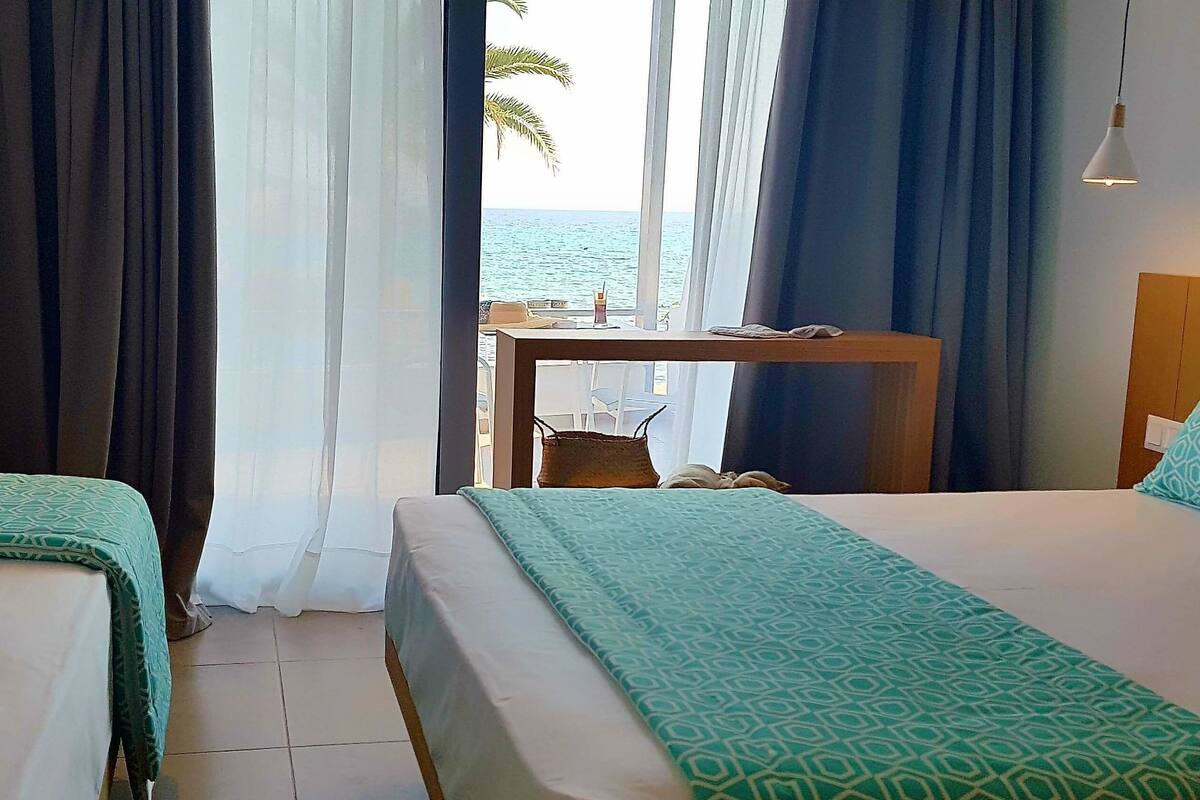 Quarto de hotel com duas camas, uma mesinha e vista para o mar.