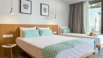 Quarto de hotel com duas camas, uma cabeceira de madeira, uma pequena mesa de cabeceira com um livro e uma janela grande com cortinas.