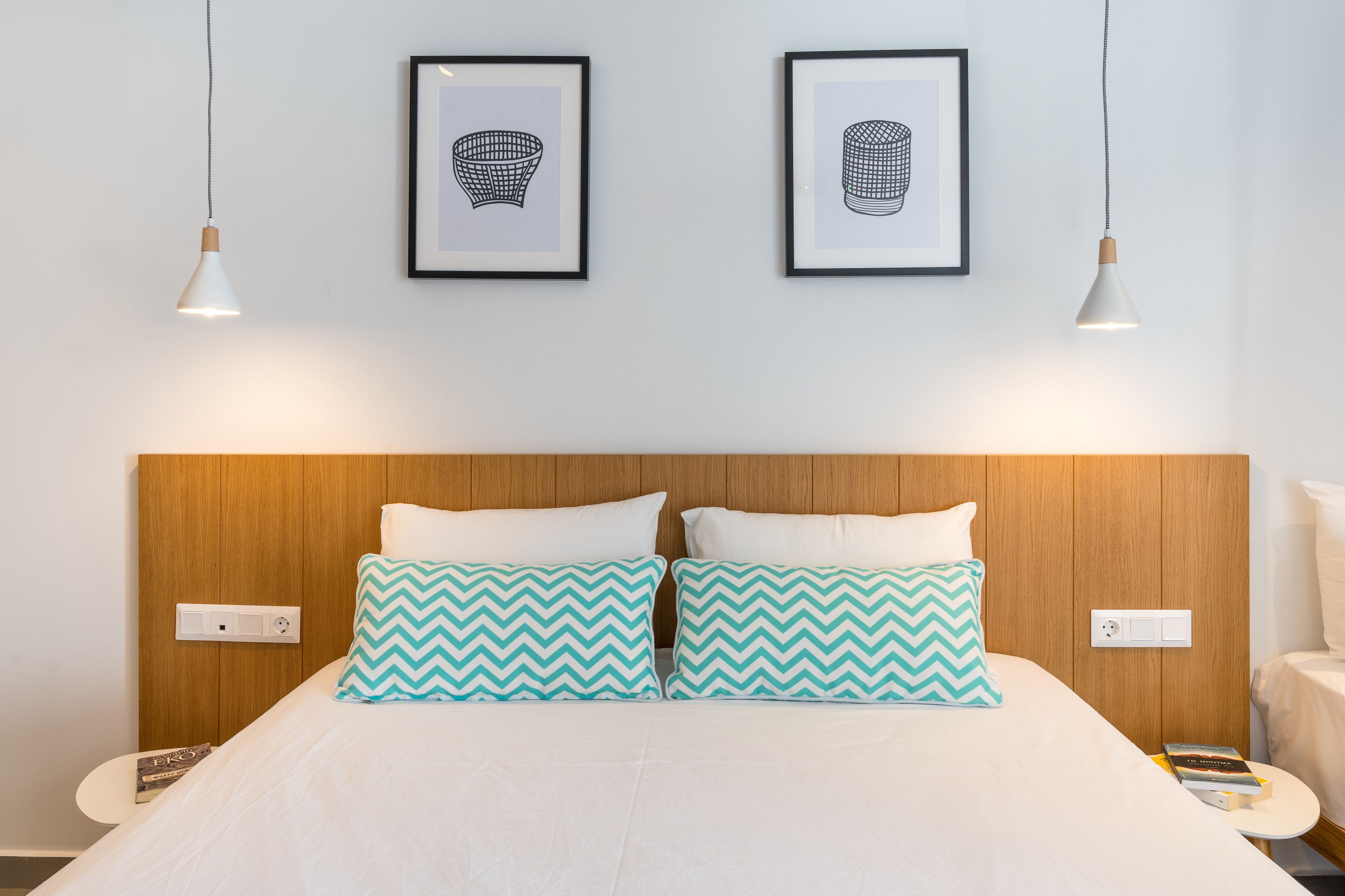 Cama bem arrumada com duas almofadas, cabeceira de madeira e duas molduras na parede.