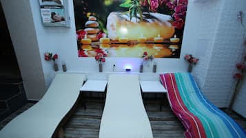 Sala de spa com duas mesas de massagem, um cartaz de tratamento de spa e um pequeno altar com velas.