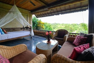 Quarto com cama, móveis de vime, mesa de vidro com um vaso e vista para o verde.