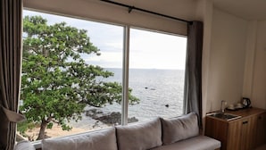Uma sala de estar moderna com uma janela ampla que oferece vista para o mar e uma árvore.