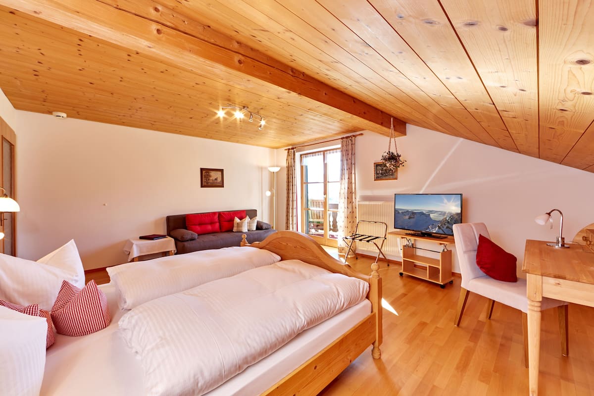 Quarto aconchegante com teto de madeira, uma cama, um sofá, uma TV e um espaço de jantar.