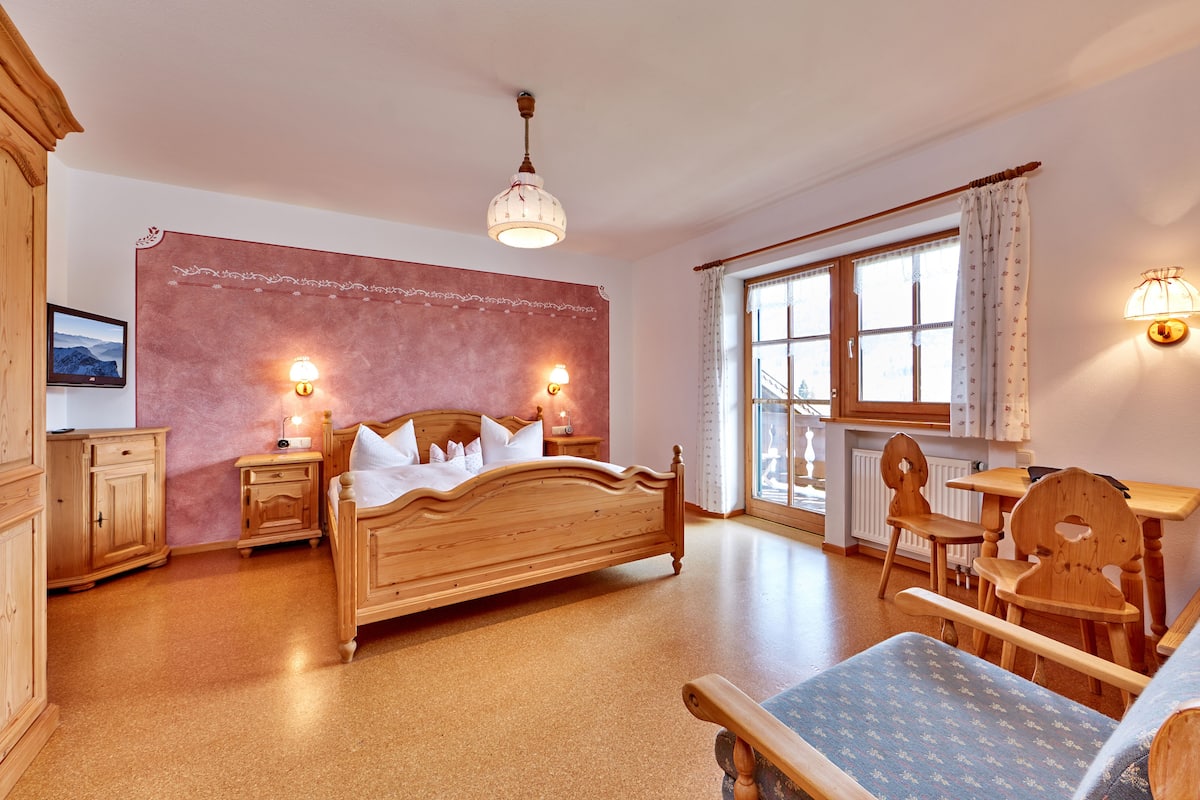Quarto com cama de madeira, mesas de cabeceira, uma cadeira e janela com cortinas.