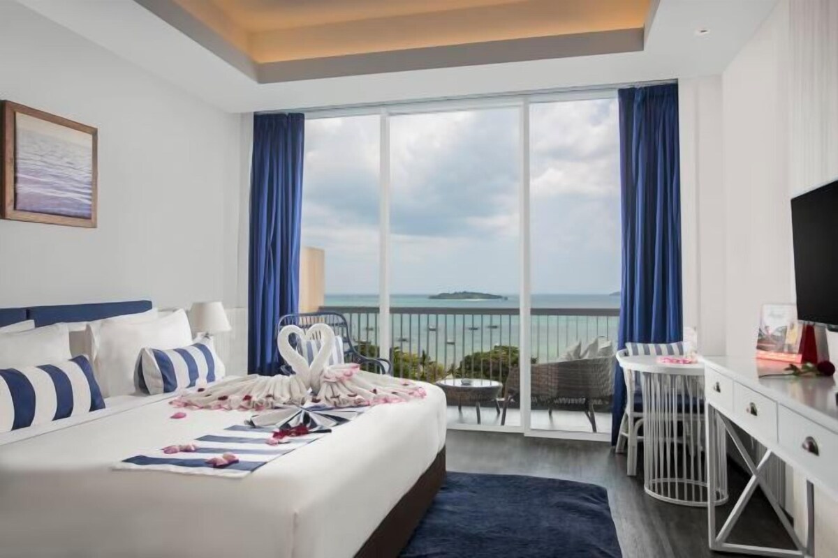 Quarto de hotel com cama, escrivaninha, cadeira e varanda com vista.
