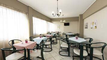 Uma sala de jantar com várias mesas e cadeiras, um candelabro e uma televisão na parede.