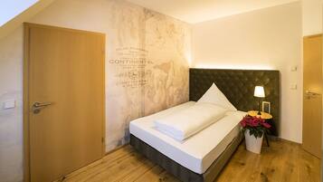 Quarto com cama, mesa de cabeceira, abajur e parede com texto.