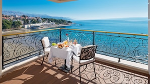 Uma varanda com mesa posta para dois, com vista para uma cidade costeira e o mar.