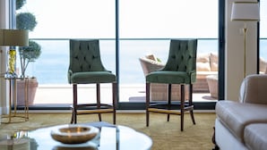Uma sala de estar moderna com uma janela grande, duas poltronas estofadas em verde, uma mesa de centro redonda, um sofá bege e um abajur.