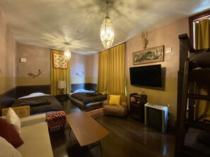 Quarto de hotel com duas camas, um sofá, uma televisão, um aquecedor e um candelabro.