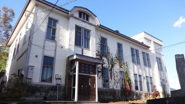 Um edifício de dois andares com fachada simétrica, grandes janelas e entrada central com porta de madeira.