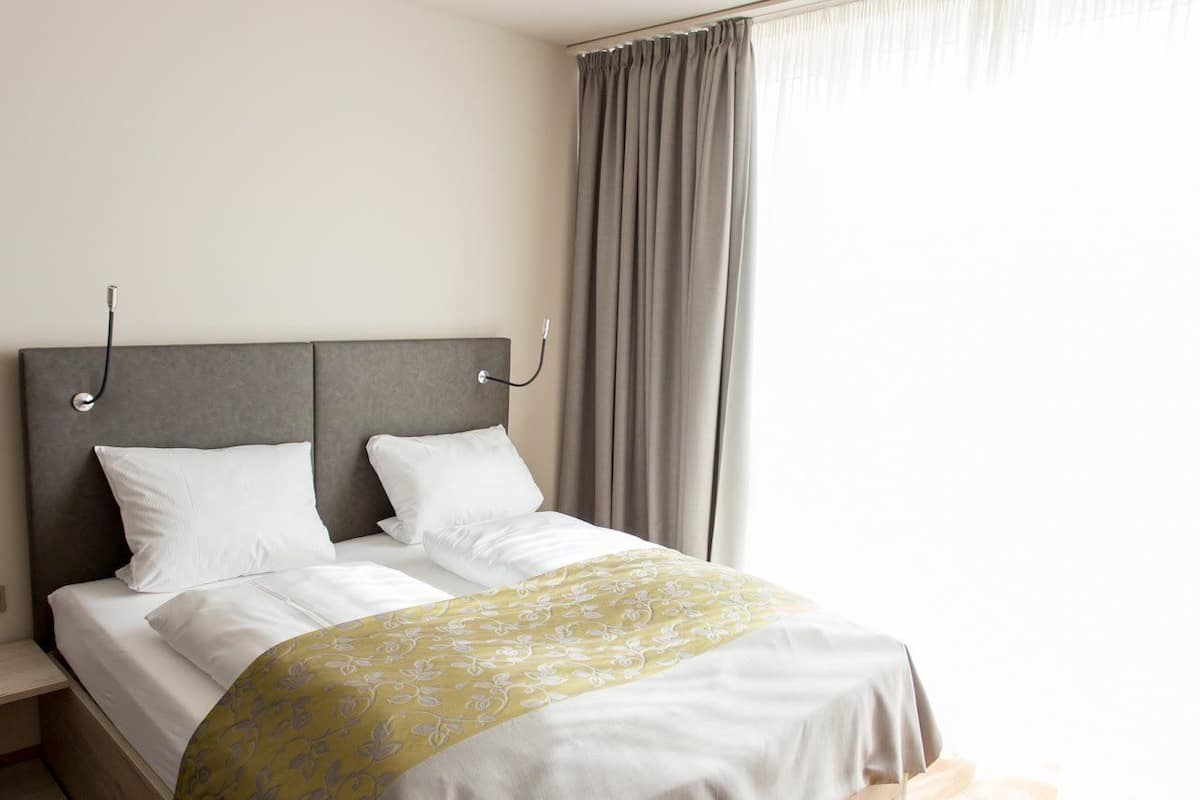 Quarto moderno com uma cama grande, cabeceira cinza e piso de madeira.