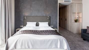Quarto de hotel moderno com uma cama grande, mesa de cabeceira, armário e um espaço de estar.