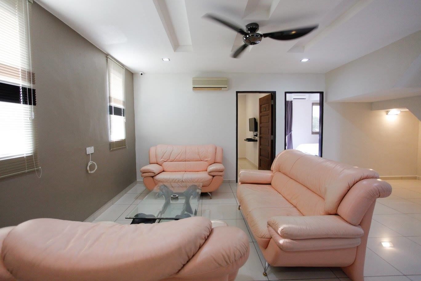 Uma sala de estar ampla, com ventilador de teto, dois sofás, uma mesa de centro de vidro e uma porta que dá para outro cômodo.