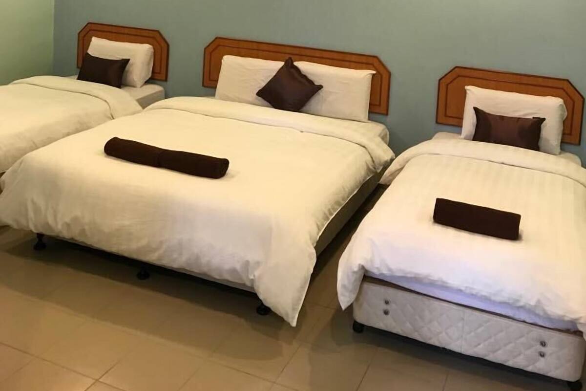 Quarto de hotel com três camas de solteiro, cada uma com cabeceira de madeira, roupa de cama branca e travesseiro marrom.