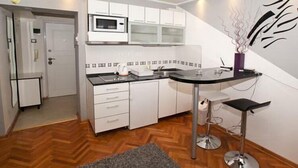 Uma cozinha compacta com armários brancos, micro-ondas e bancada preta.