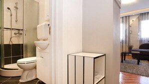 Um banheiro moderno com chuveiro em gabinete de vidro, vaso sanitário e um pequeno armário branco.