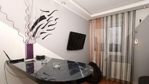Quarto moderno com mesa de vidro curva, televisão de tela plana e um detalhe decorativo na parede.