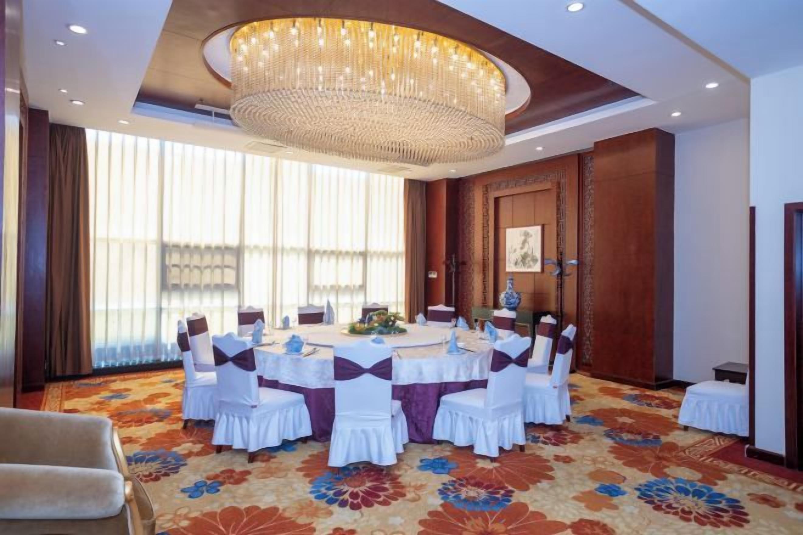 Uma sala de conferências com uma mesa redonda, cadeiras brancas e um lustre.