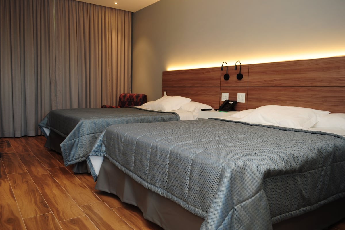 Quarto de hotel com duas camas, piso de madeira e cabeceira com luminária.