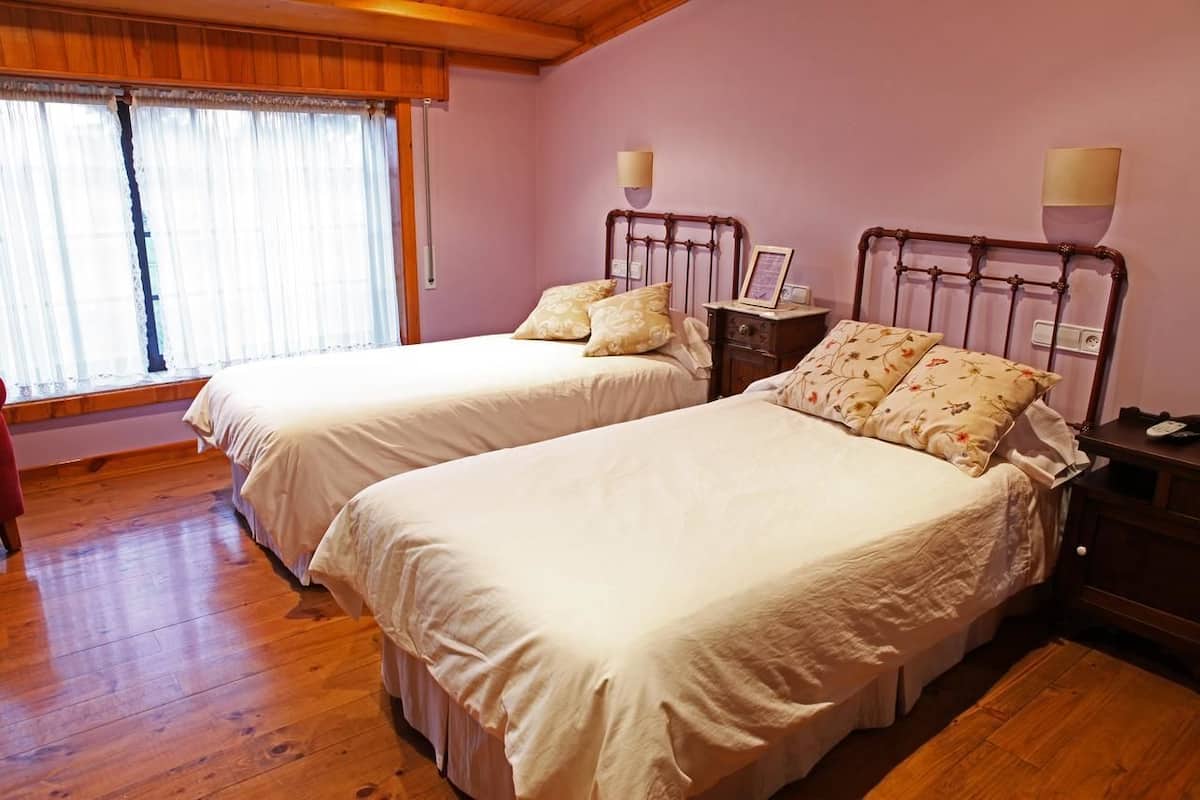 Quarto com duas camas, piso de madeira, janela com cortinas e abajures.