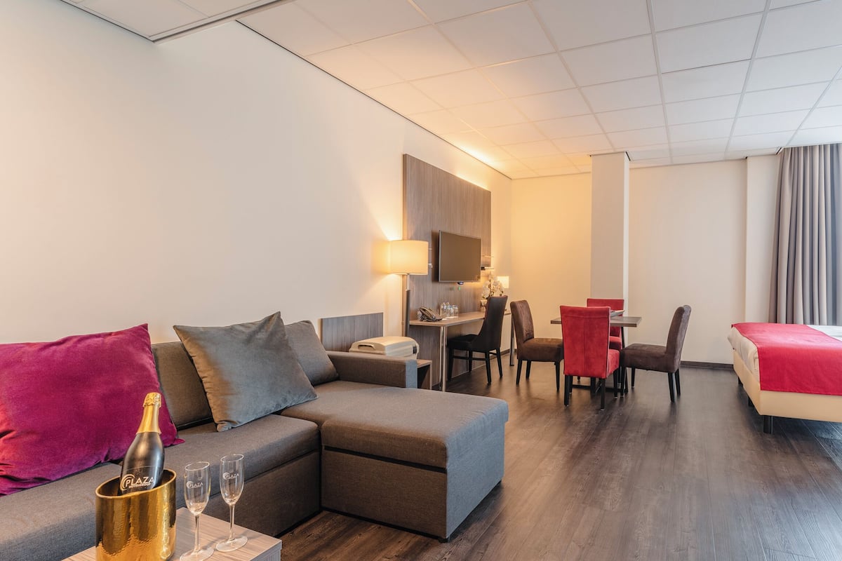 Quarto de hotel moderno com sofá, cama, escrivaninha e área de refeições.