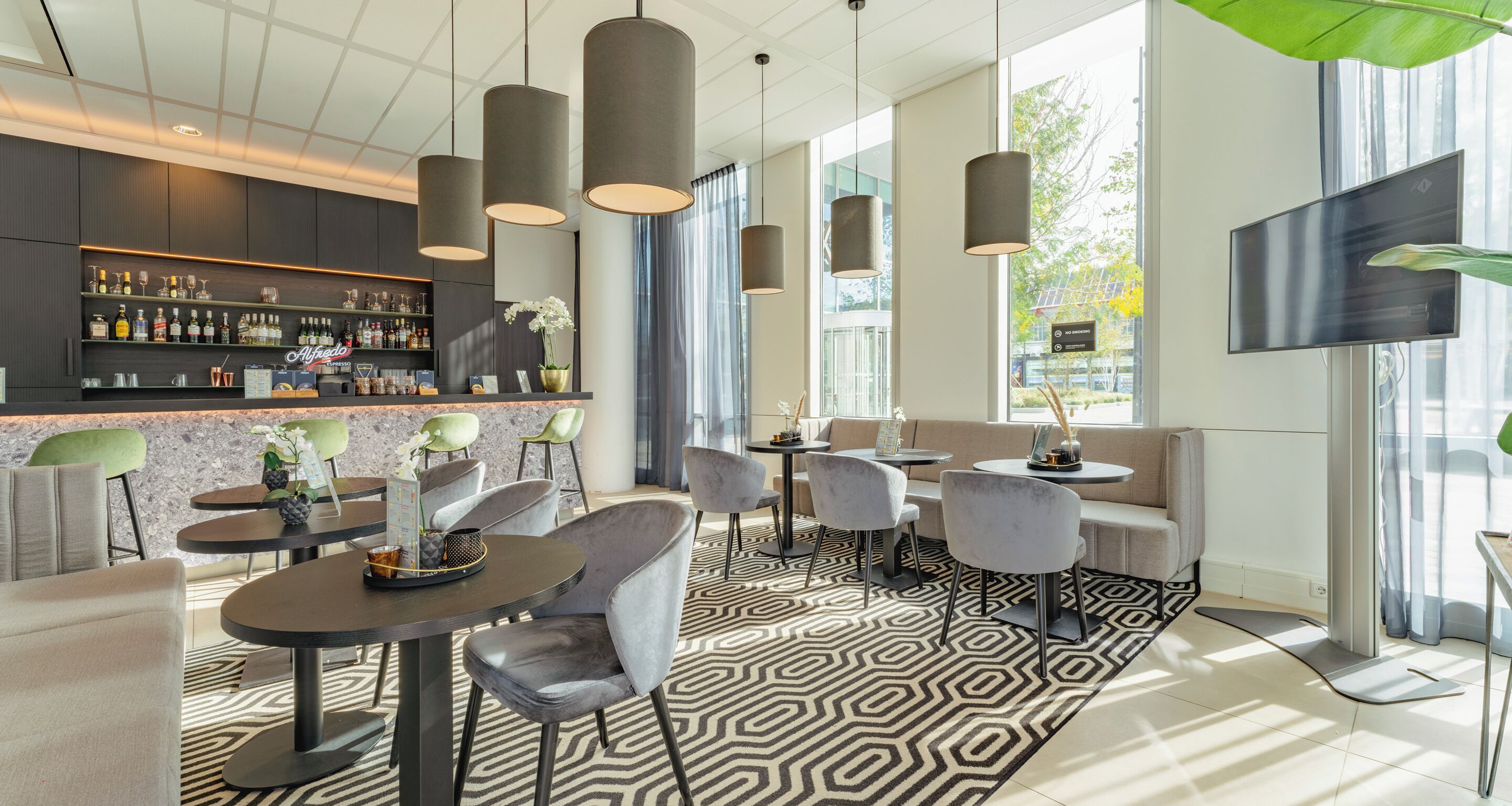 Uma área de bar moderna com um balcão comprido, diversas opções de assento incluindo mesas redondas e cadeiras, e um chão estampado.
