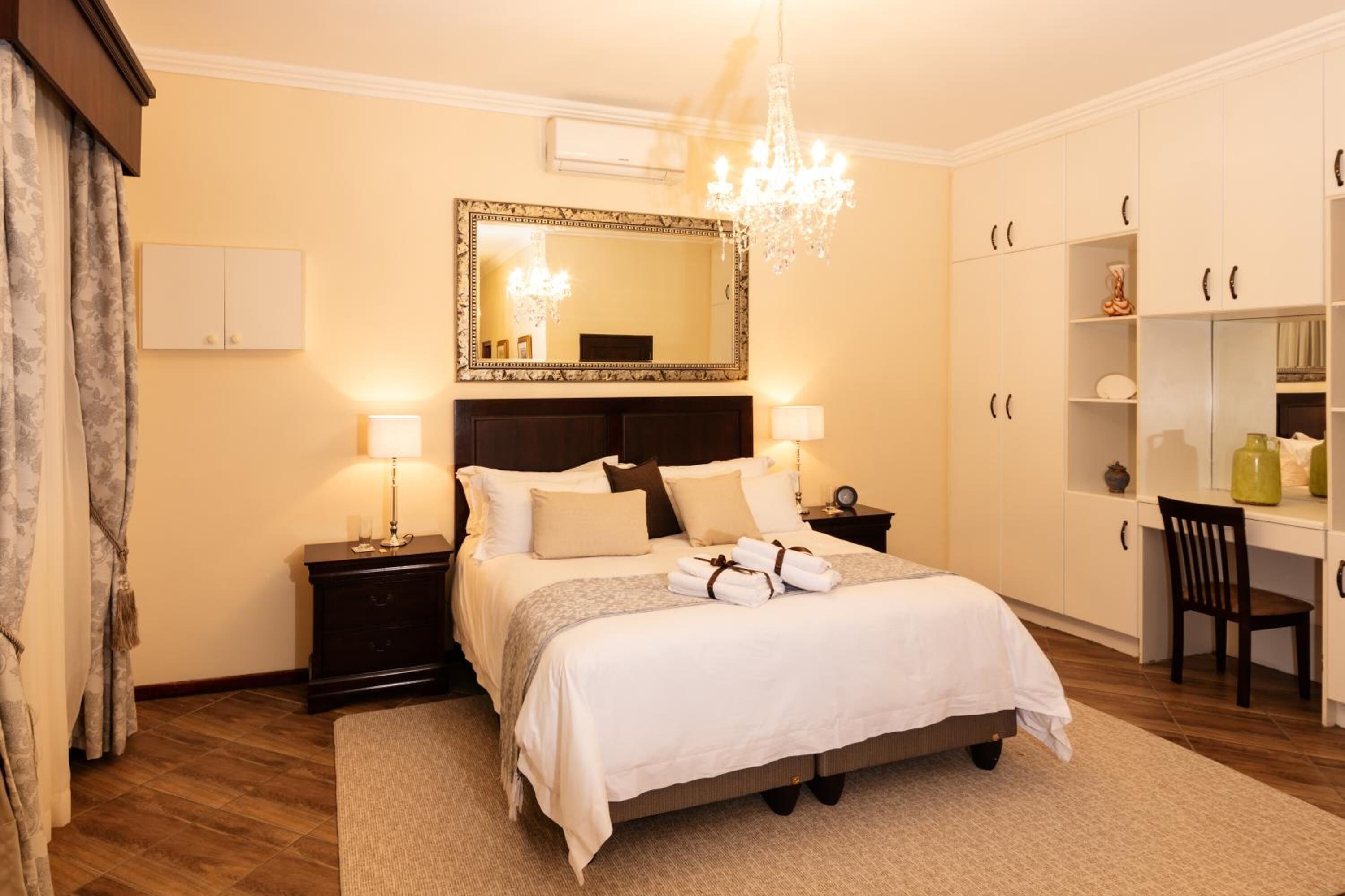 Quarto de hotel com cama grande, abajures, lustre, guarda-roupa e escrivaninha com cadeira.