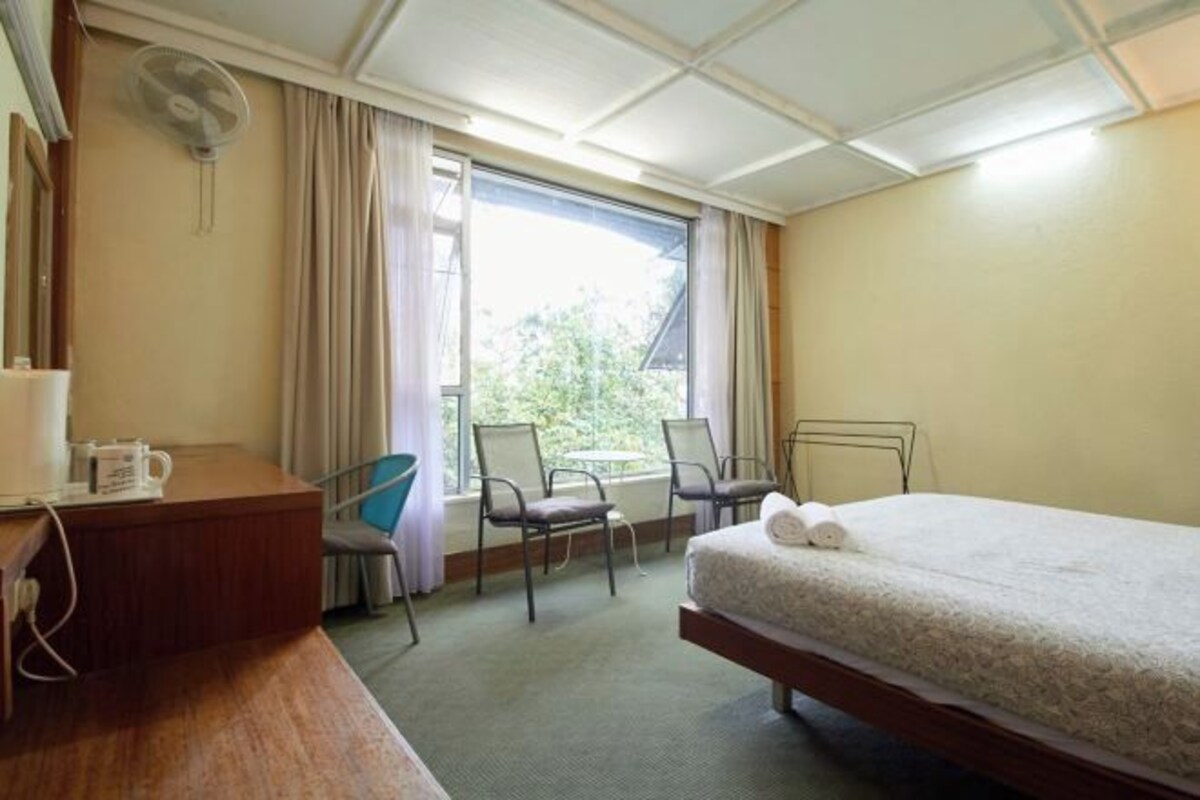 Quarto de hotel com cama, escrivaninha, cadeira e janela com cortinas.