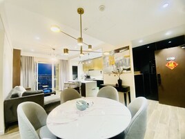 Uma sala de estar moderna com uma mesa de jantar redonda, sofás cinzentos e vista para a cidade à noite.