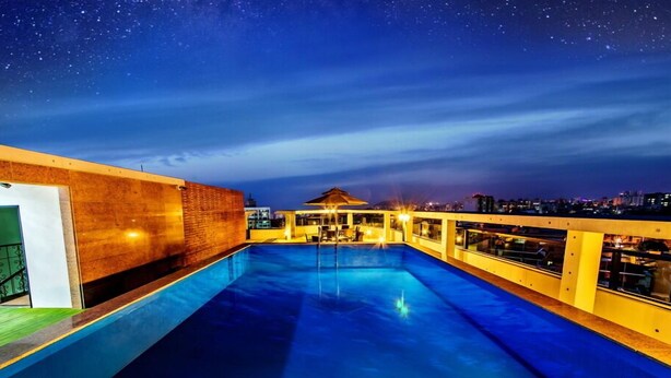 Piscina no terraço com vista para a cidade à noite, área de estar coberta e um bar.
