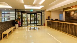 Uma área de recepção de hotel com design moderno, com um balcão de atendimento, um banco e entrada por porta de vidro.