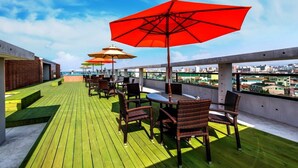 Terraço no telhado com área de estar externa, guarda-sóis e vista para a cidade.