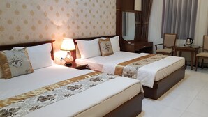 Quarto de hotel com duas camas, mesa de cabeceira com abajur, escrivaninha de madeira e uma cadeira.