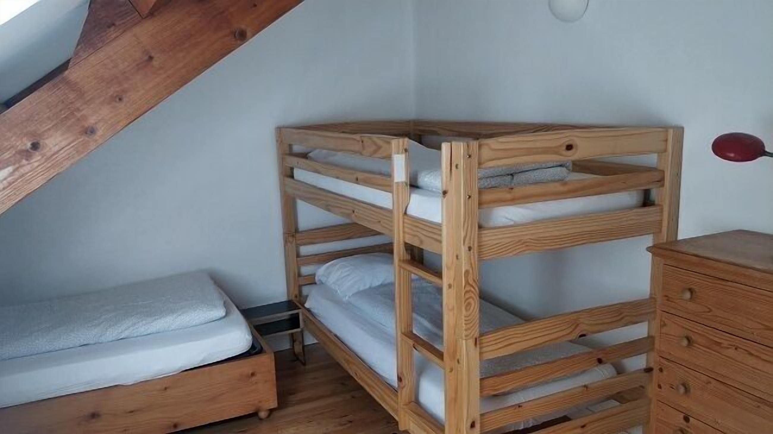 Um quarto com uma cama beliche de madeira, uma cômoda pequena de madeira e um colchão branco no chão.